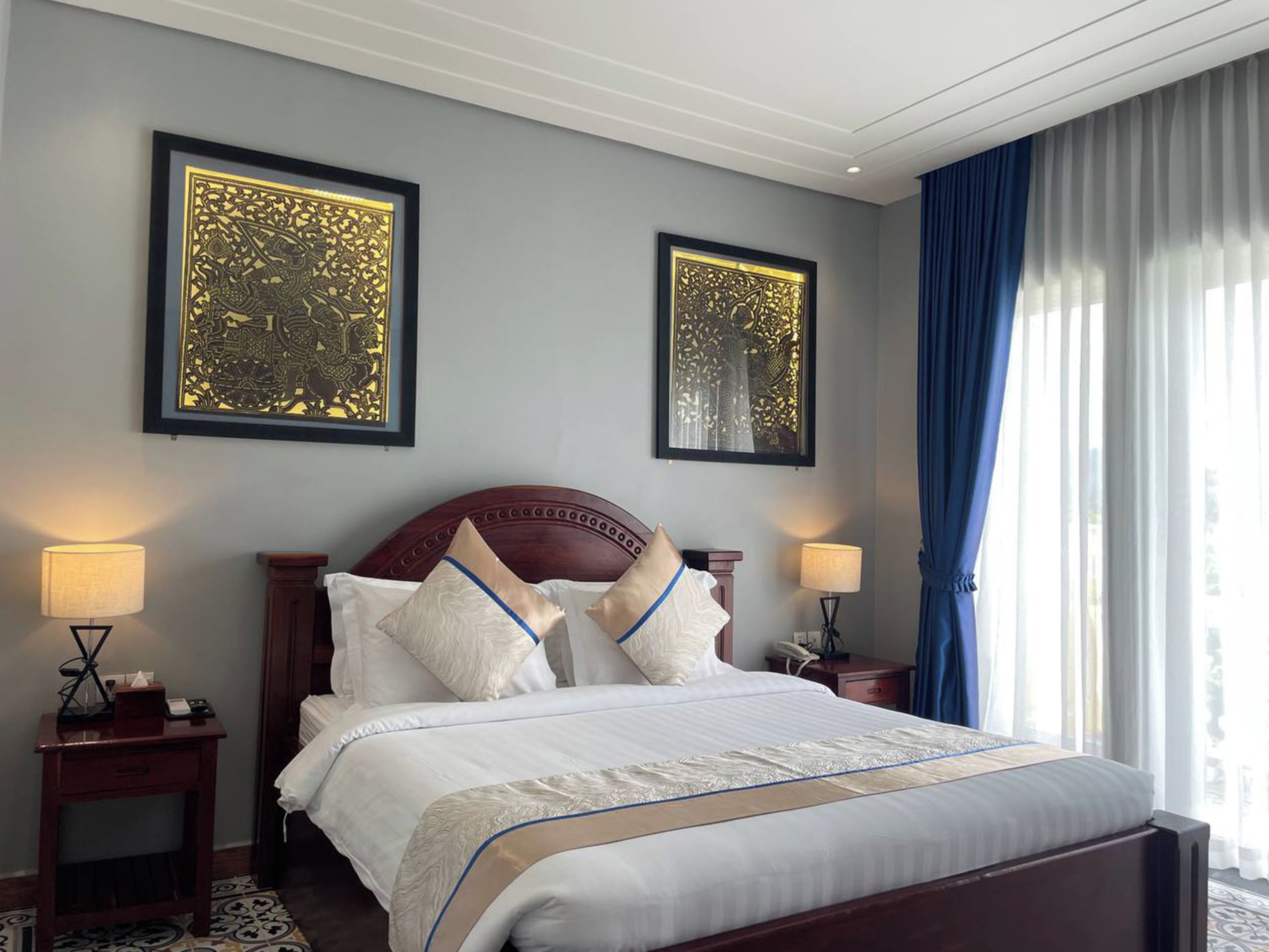 Quarto de hotel com uma cama grande, duas mesas de cabeceira com luminárias, uma cabeceira e duas obras de arte emolduradas na parede.