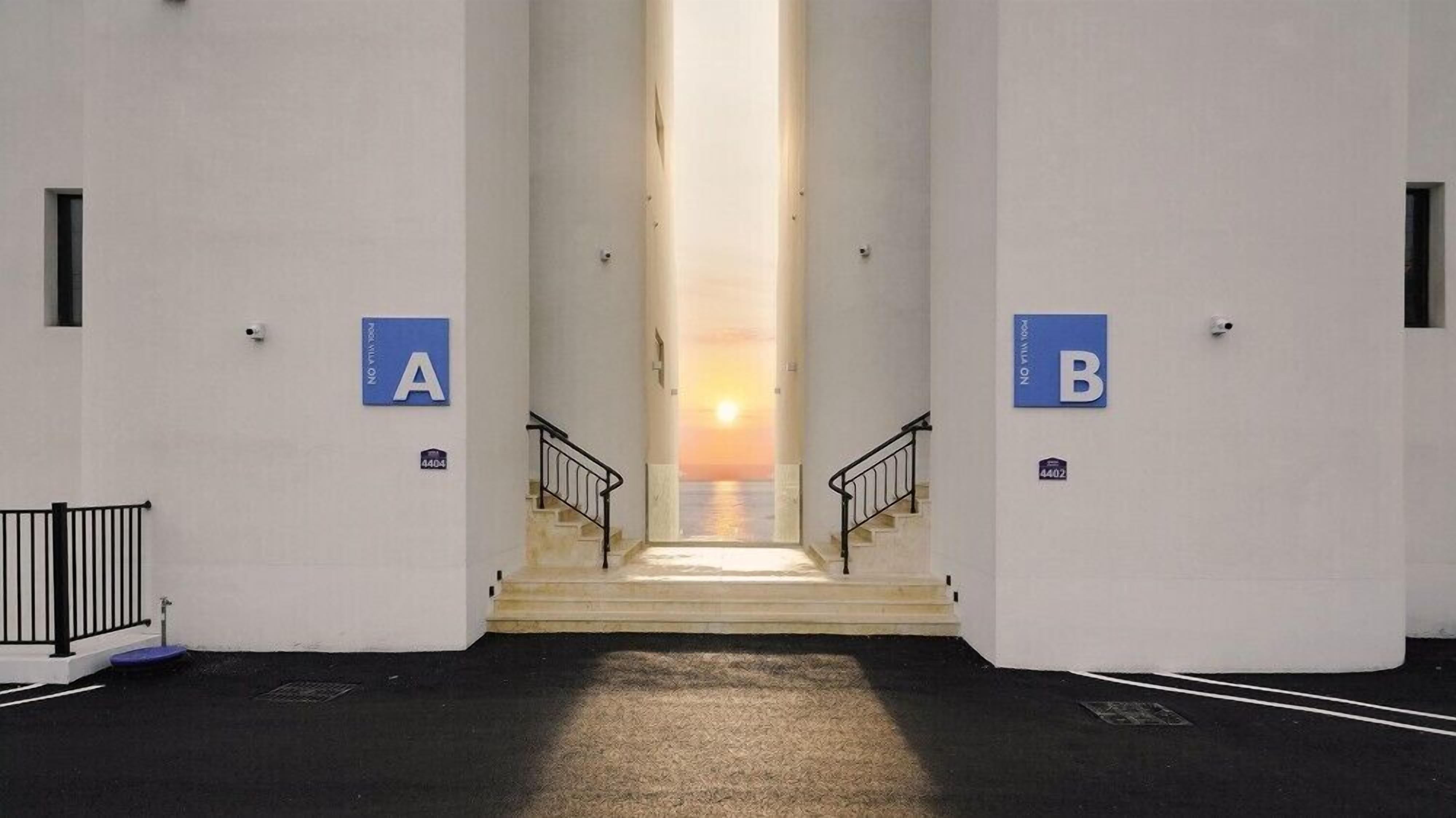 Um corredor com vista para o pôr do sol através de uma abertura central, que leva a uma escadaria.