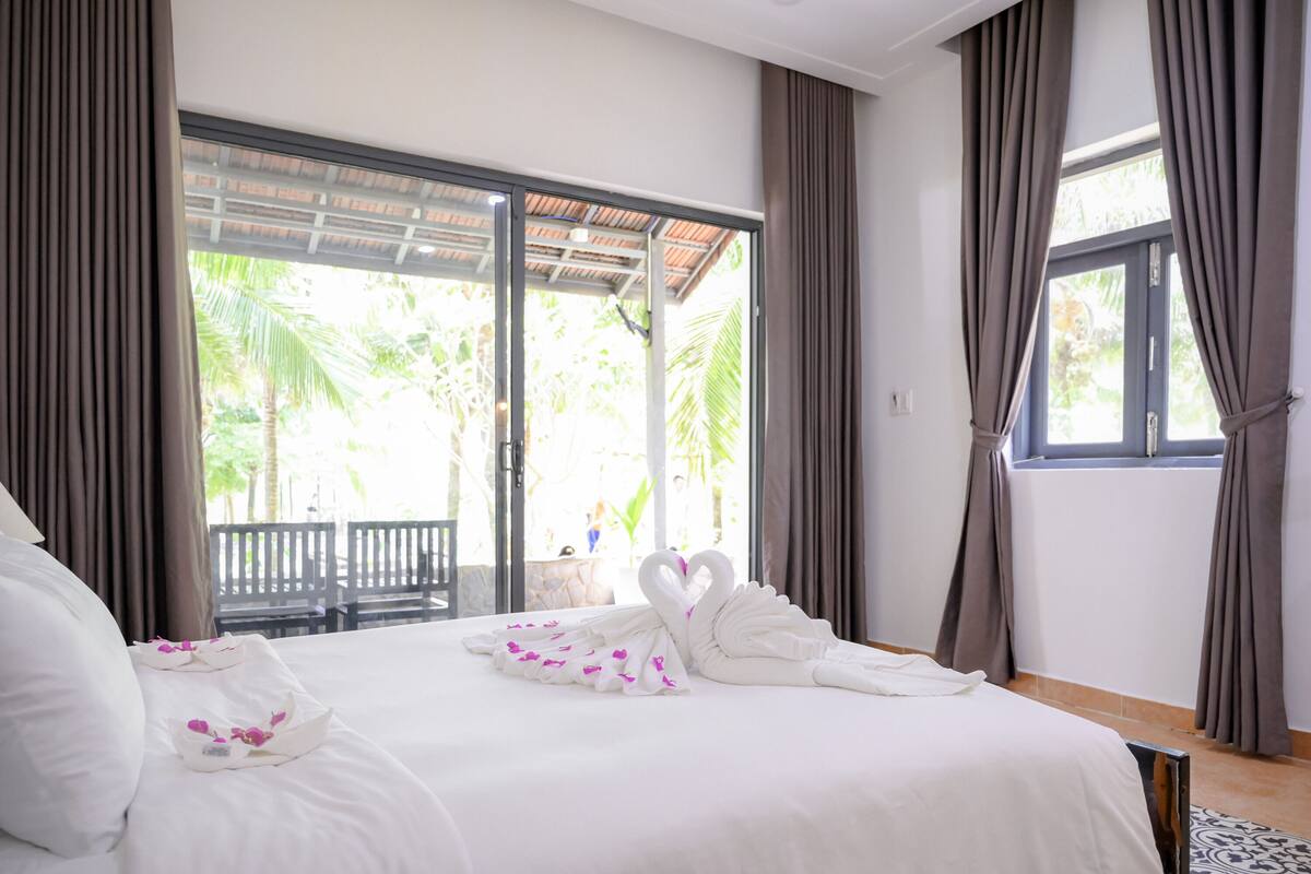 Quarto de hotel com cama, cortinas e vista para palmeiras.