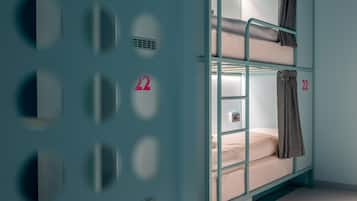 Uma cama beliche com o número '22' na parede, uma janela e uma grade de ventilação.