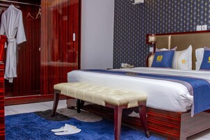 Quarto de hotel com cama grande, um banco, um guarda-roupa e um par de chinelos no chão.