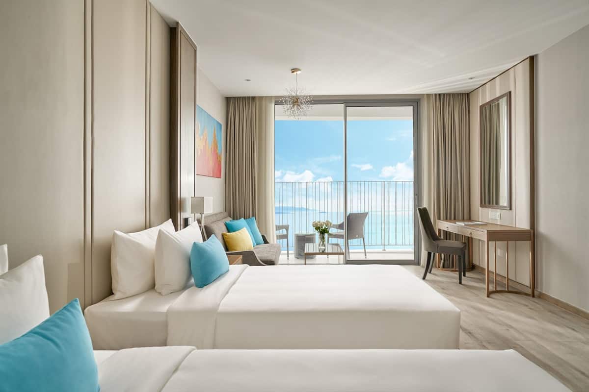 Quarto de hotel com cama grande, escrivaninha e vista para o oceano.