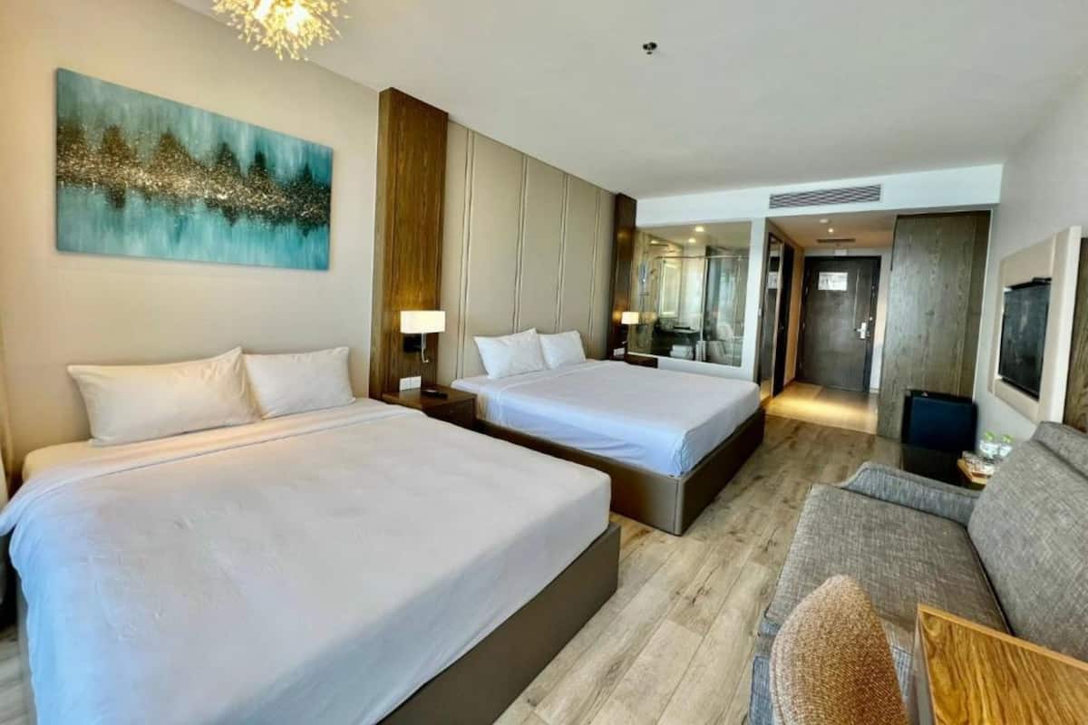 Quarto de hotel com duas camas, um sofá, uma pintura grande e um candelabro.