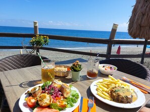 Uma mesa posta com comida, bebidas e vista para a praia.