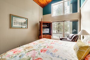 Quarto com uma cama grande, um armário de madeira, uma televisão e uma janela com vista para árvores.
