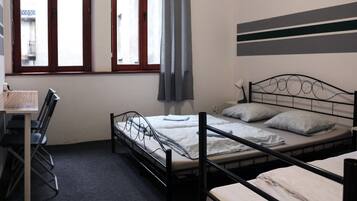 Quarto com cama, escrivaninha e cadeira. Há uma janela com cortinas.