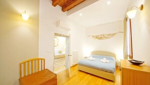 Quarto com cama, mesa de cabeceira e uma cadeira. Uma porta dá acesso a outro cômodo.