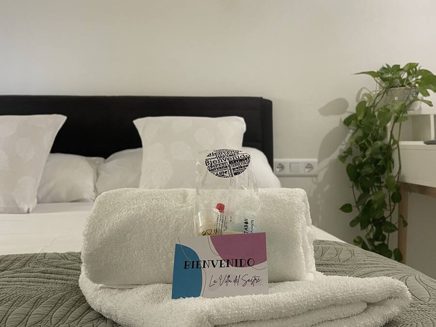 Cama bem arrumada com uma toalha branca dobrada e uma sacola de boas-vindas.