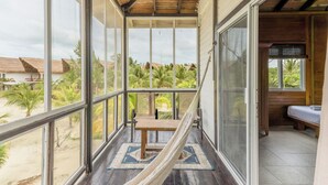 Uma varanda com rede, uma mesa de madeira e vista para palmeiras e edifícios com telhados de palha.