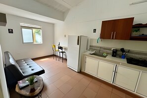 Cozinha compacta com armários brancos, geladeira e área de jantar com sofá preto e duas cadeiras.