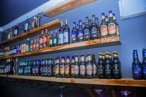 Prateleiras repletas com diversas garrafas de bebidas alcoólicas, incluindo marcas como Guinness e Castle.