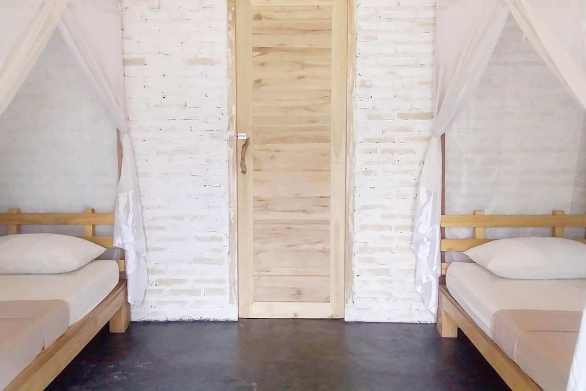 Quarto com duas camas de madeira, roupa de cama branca e uma parede de tijolos brancos.