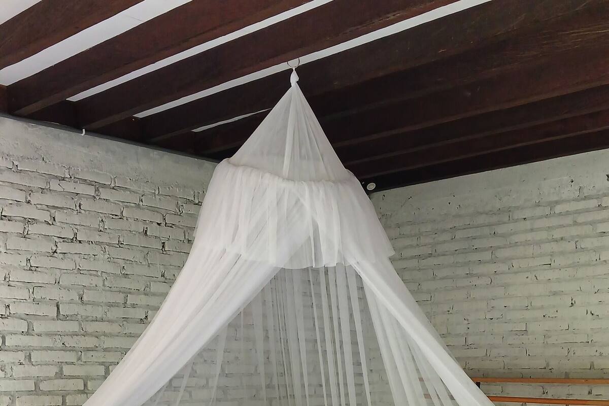 Uma cama com estrutura de madeira, roupa de cama branca e um dossel branco.