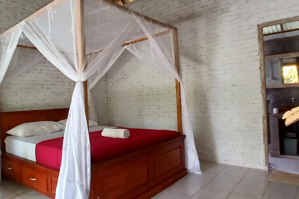 Quarto com cama de madeira, uma cadeira e cortina branca.