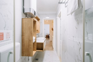 Uma casa de banho moderna com toucador de madeira, uma pia branca e zona de duche.