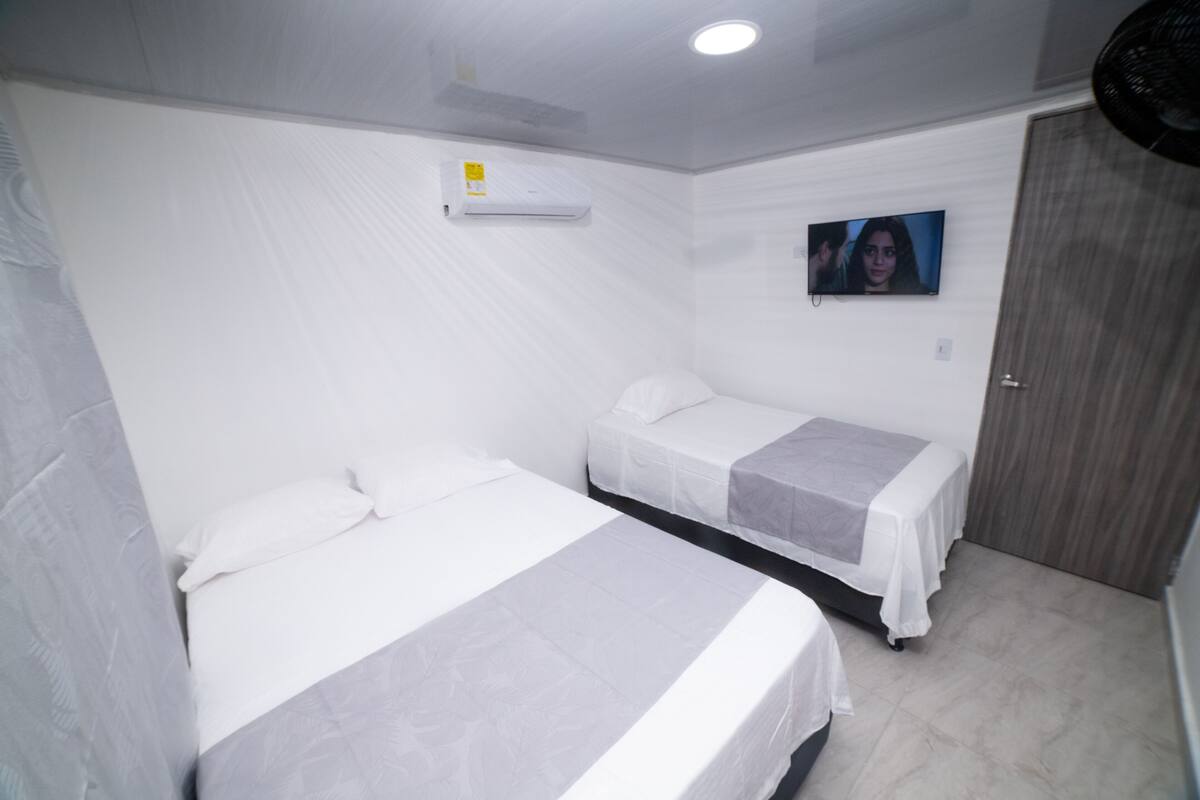 Quarto de hotel com duas camas, uma televisão na parede e uma porta.