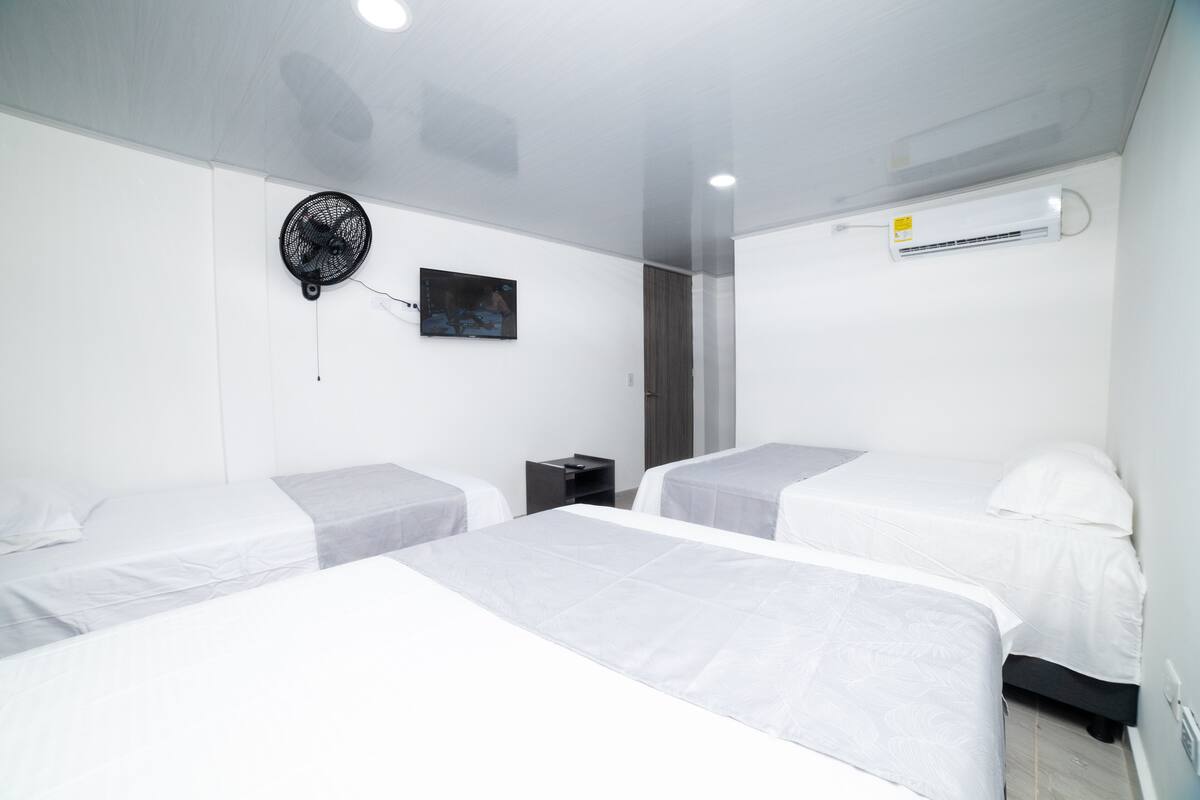 Quarto de hotel com duas camas, um ventilador de teto, ar condicionado e uma pequena mesa com uma televisão.