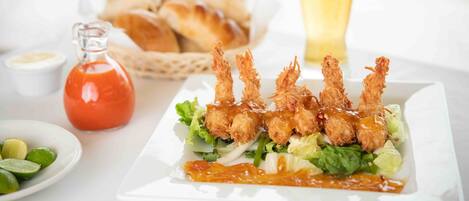 Um prato de comida frita com molho para acompanhar, um copo de cerveja e uma cesta de pão.