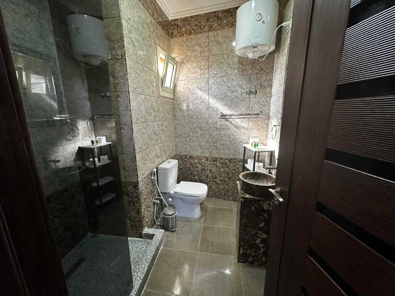Casa de banho com sanita, lavatório, chuveiro e parede de mármore.