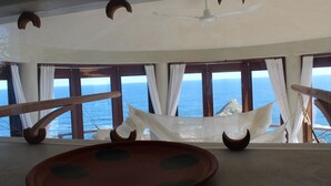 Quarto com vista para o oceano, um ventilador de teto e uma rede.