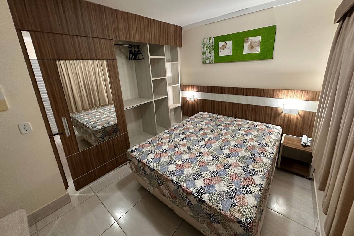 Quarto com cama, guarda-roupa, espelho e um adorno verde na parede.