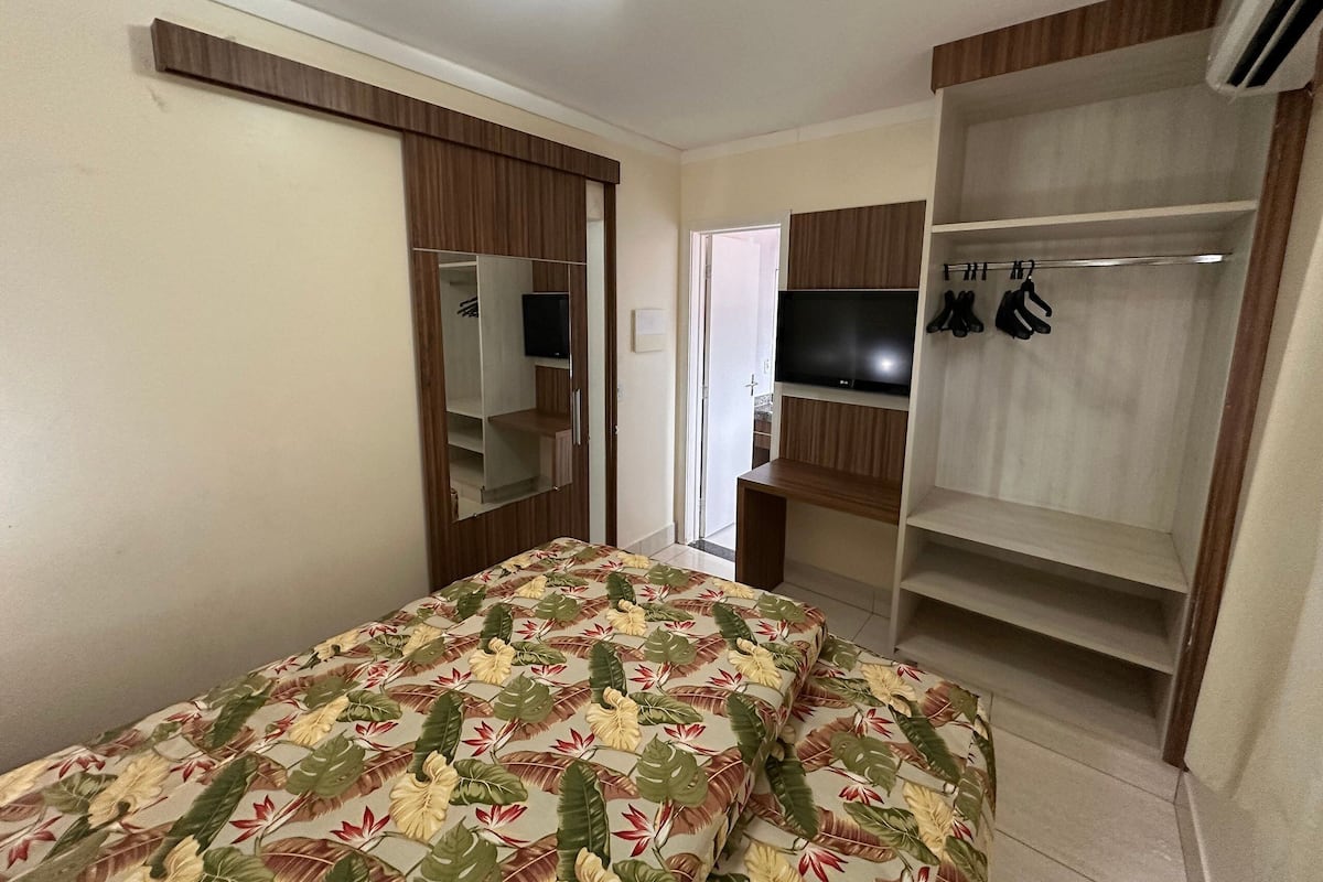 Quarto com cama, guarda-roupa, televisão e espelho.