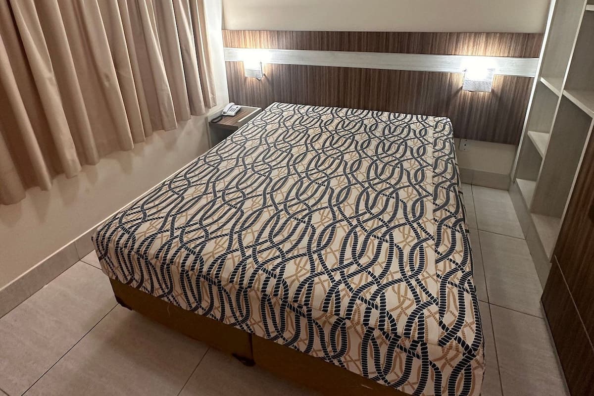 Um quarto moderno com colcha estampada, telefone fixado na parede e um objeto decorativo sobre a cama.