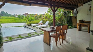 Uma área externa coberta com piscina, espreguiçadeiras e uma mesa de madeira.