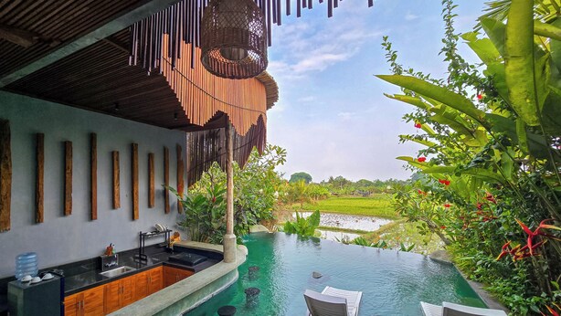 Piscina infinita com área de bar, cercada por vegetação exuberante e vista para um campo de arroz.