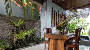 Uma mesa de jantar de madeira com cadeiras, rodeada por plantas em vasos e uma parede de pedra.