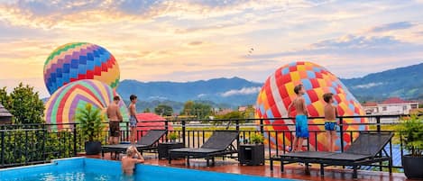 Piscina com espreguiçadeiras e balões de ar quente ao fundo.