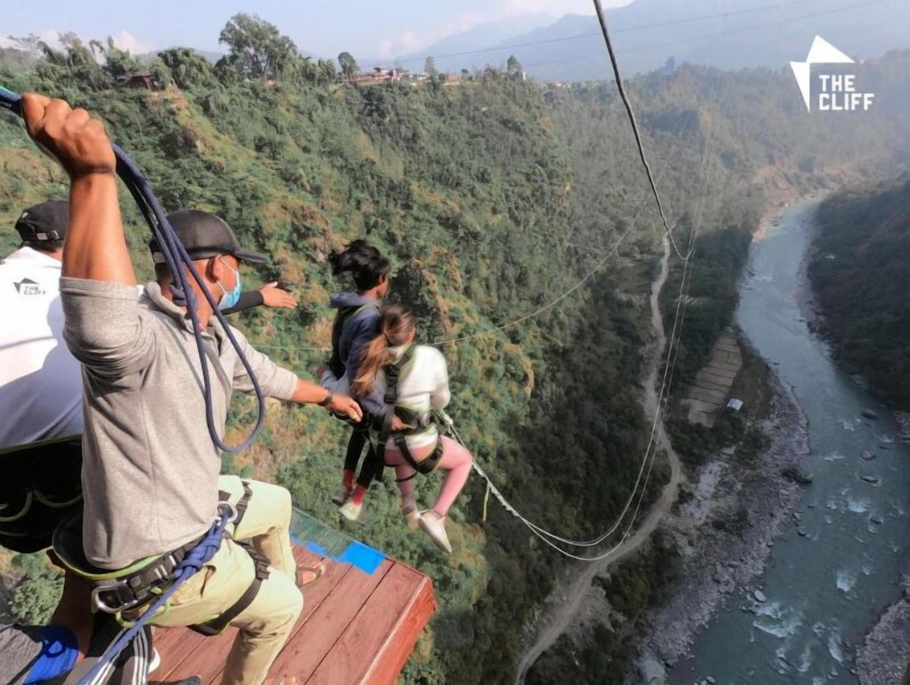 Uma pessoa faz bungee jump com um instrutor segurando um arnês de segurança.