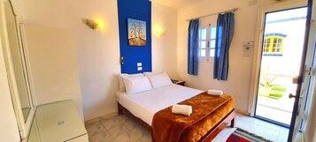 Quarto com cama, parede azul, janela com cortinas e porta que dá para o exterior.