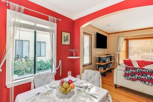 Uma área de refeições com uma mesa posta para quatro pessoas, um sofá branco e uma televisão ao fundo.