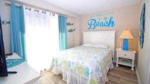Quarto com cama, cortinas, mesa de cabeceira com abajur e um objeto decorativo na parede.