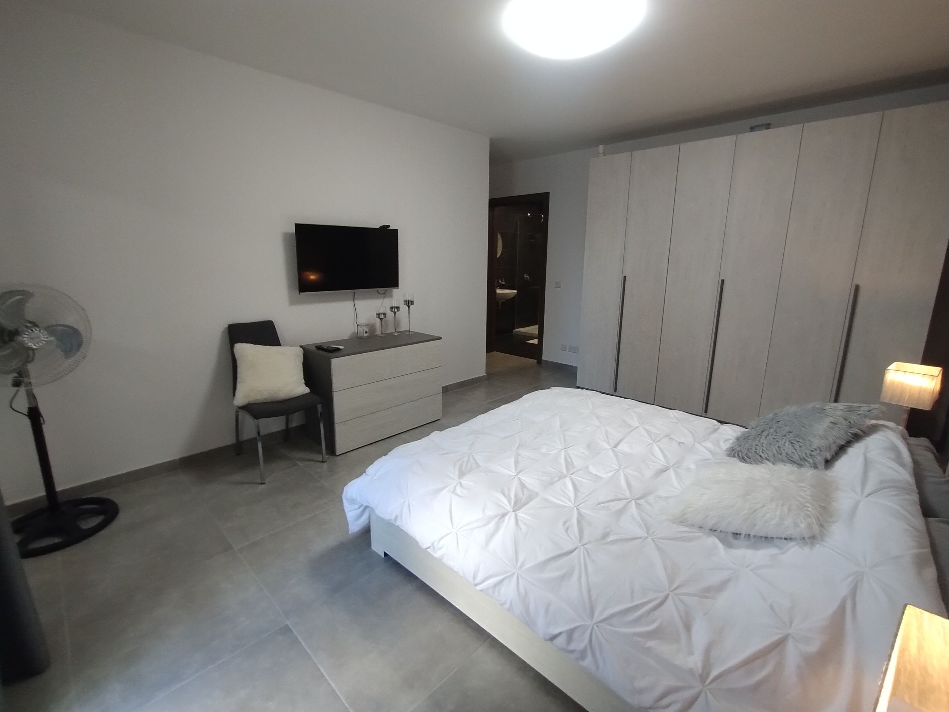 Quarto moderno com cama, escrivaninha, cadeira, televisão e guarda-roupa.