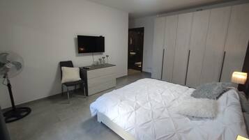 Quarto moderno com cama, escrivaninha, cadeira, televisão e guarda-roupa.