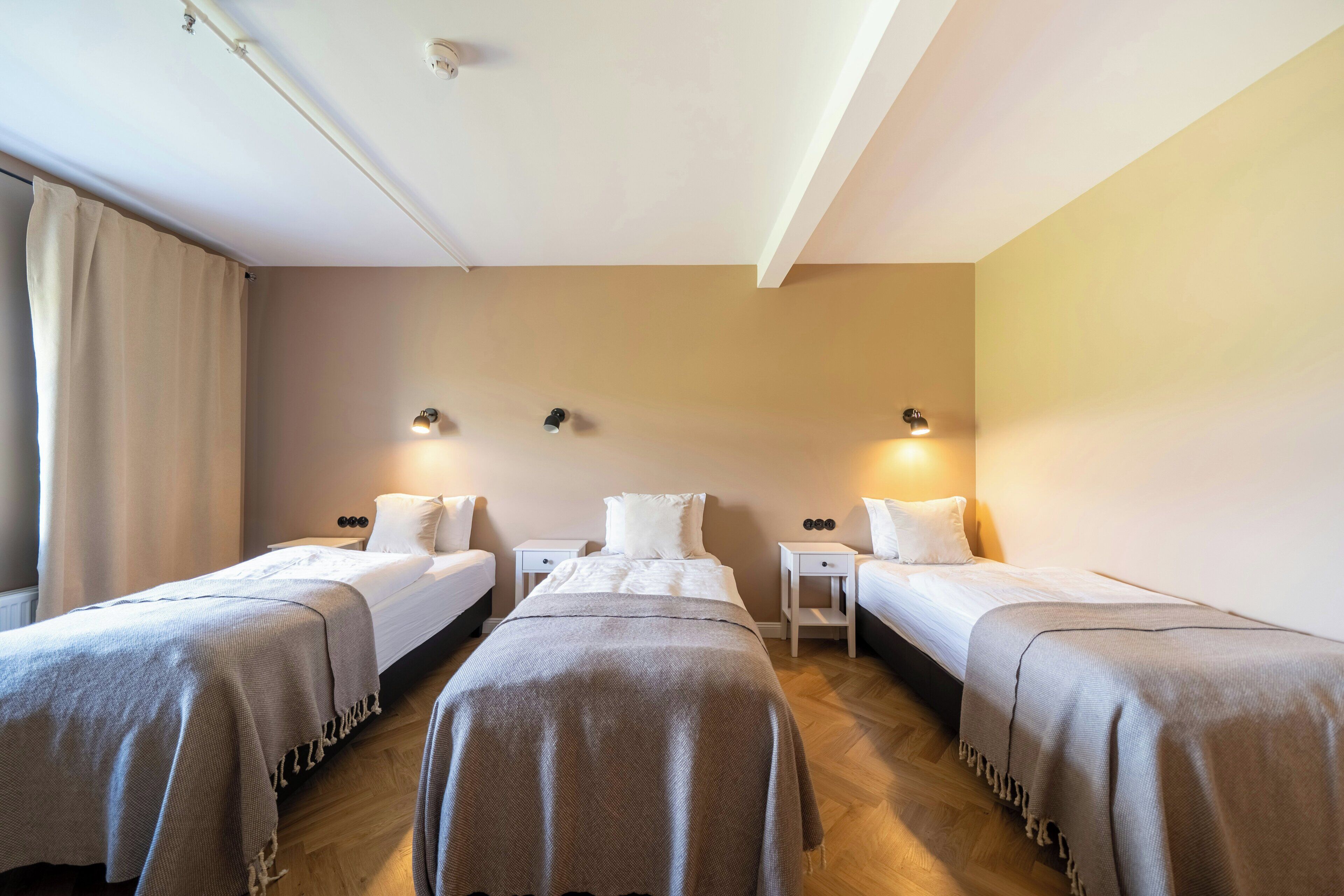 Quarto de hotel com duas camas de solteiro, uma mesinha, duas mesas de cabeceira e um lustre no teto.