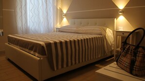 Uma cama bem arrumada com roupa de cama listrada, uma mesa de cabeceira com abajur e uma bolsa em uma mesinha.