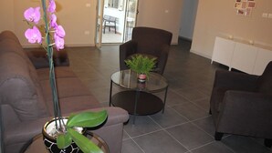 Uma sala de estar com sofá, poltronas, mesa de centro de vidro e uma planta, além de um armário.
