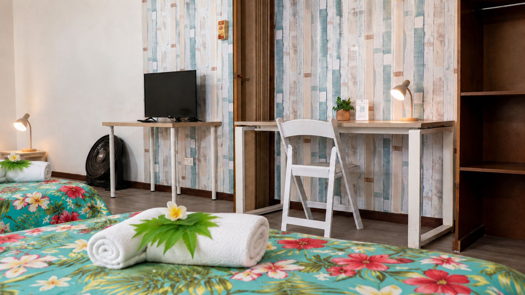 Quarto de hotel com cama, escrivaninha e cadeira, televisão e parede com padrão listrado.