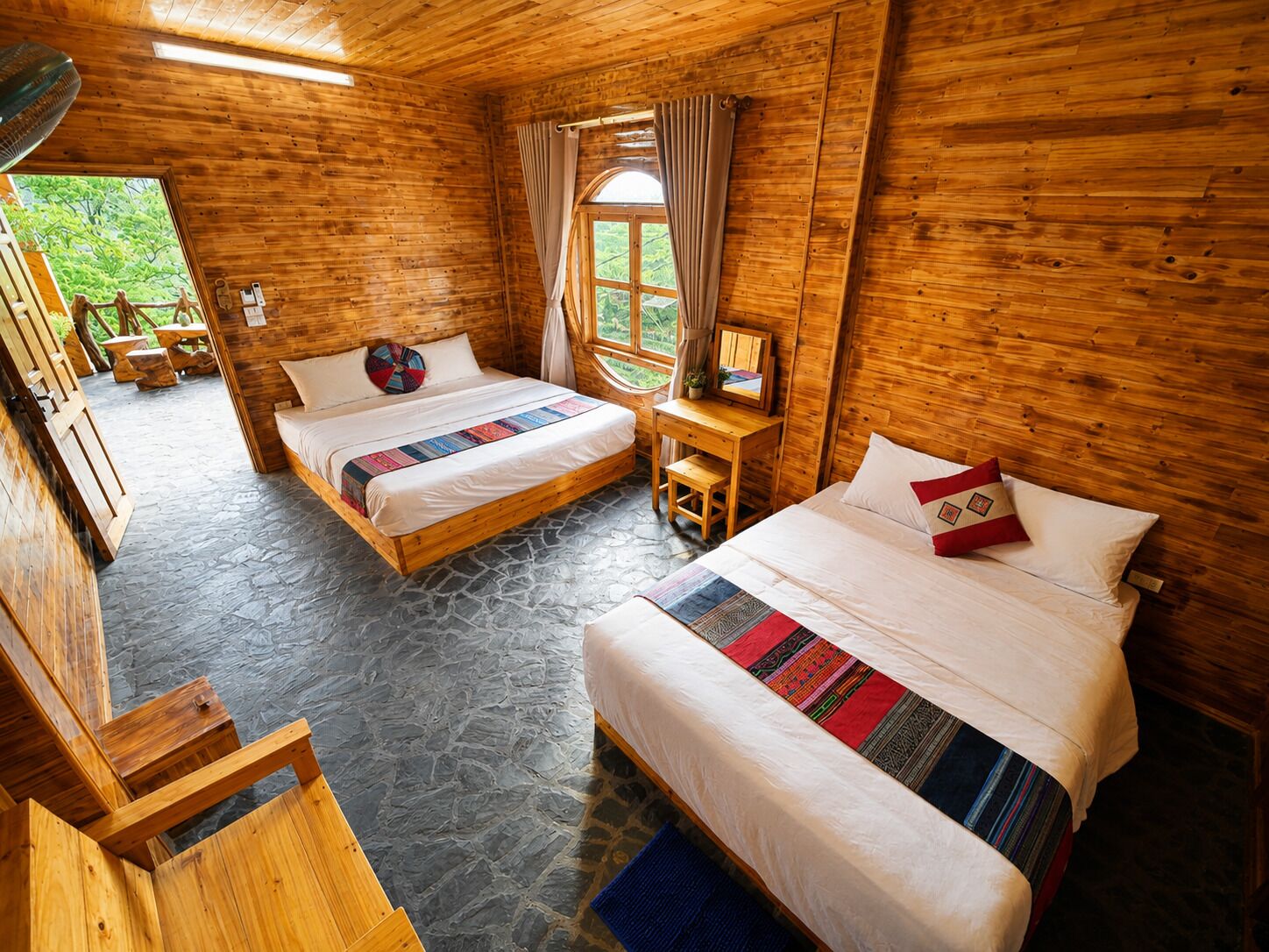 Uma cabana de madeira com duas camas, uma escrivaninha pequena e uma janela com cortinas.