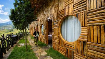 Fileira de edifícios em estilo de cabana de toras, com janelas redondas, um caminho de pedra e uma pessoa vestida com traje tradicional.