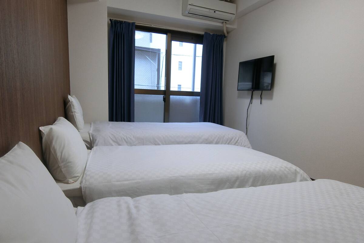 Quarto de hotel com duas camas, uma televisão na parede e uma janela com cortinas.