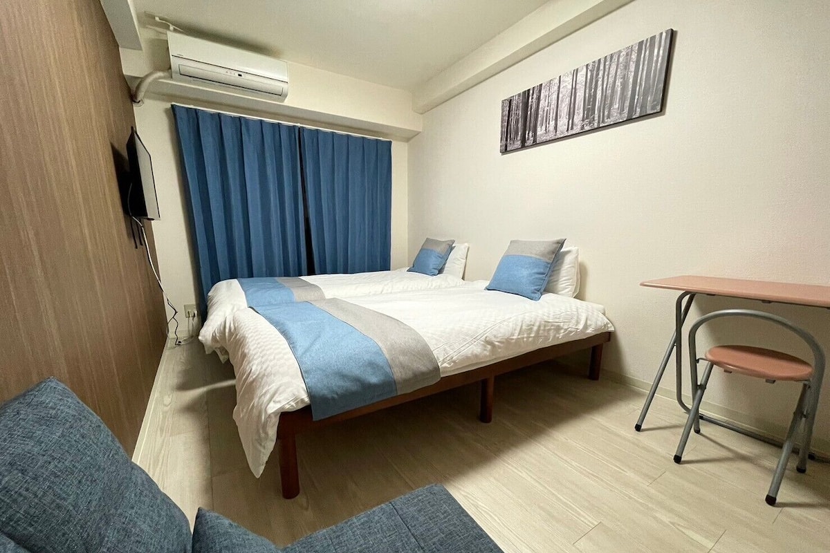 Quarto de hotel com cama, escrivaninha, cadeira e um quadro na parede.