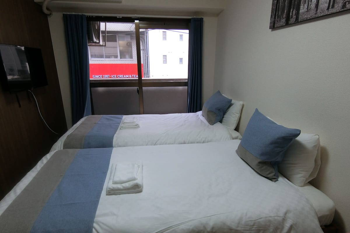 Quarto de hotel com duas camas, televisão e janela com vista para um edifício.