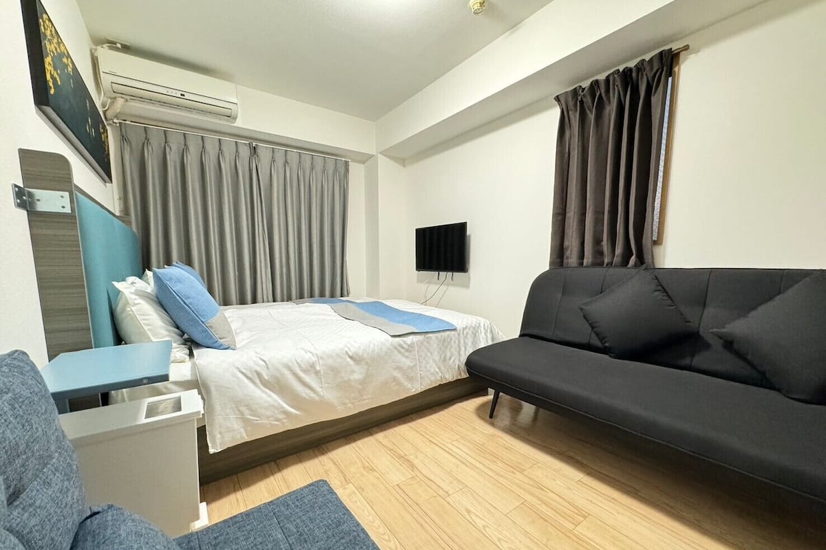 Um quarto com cama, sofá, televisão e escrivaninha.