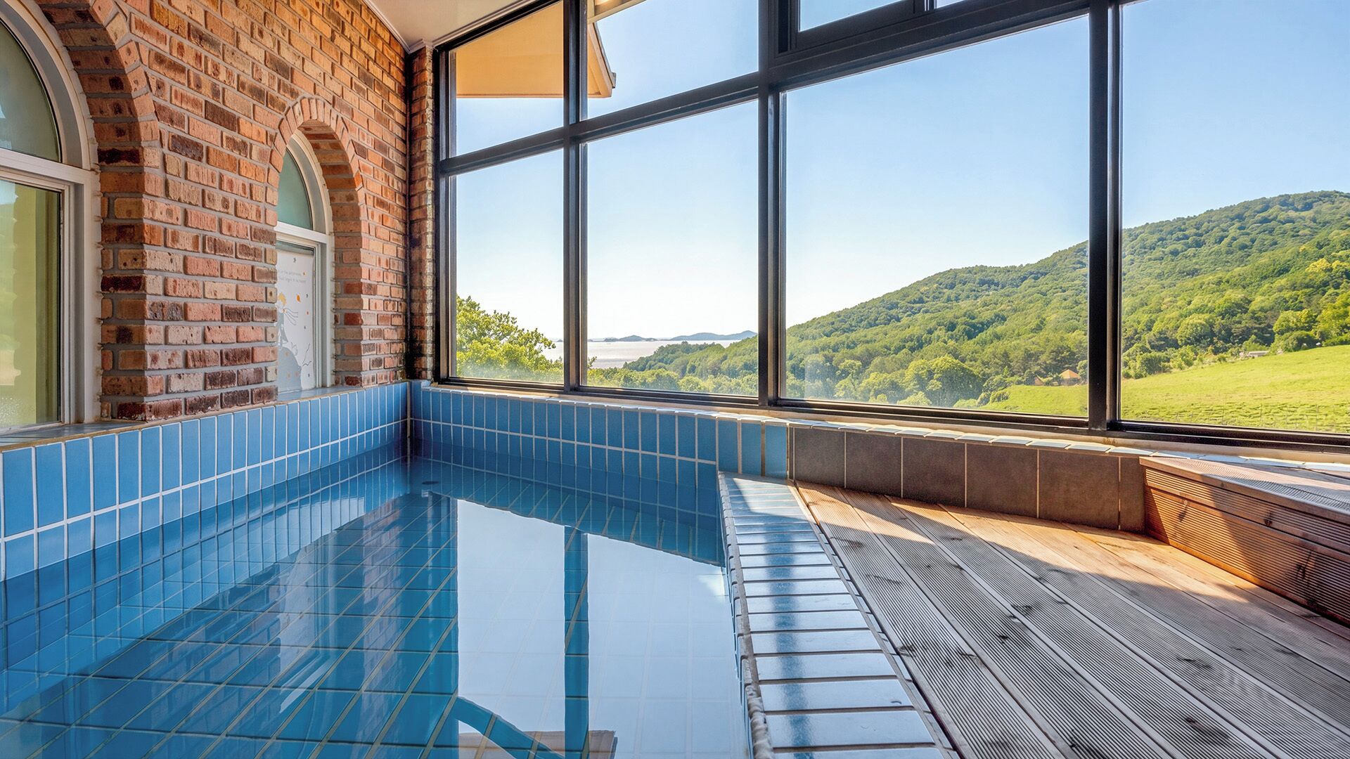 Piscina com vista para uma paisagem verde através de grandes janelas.
