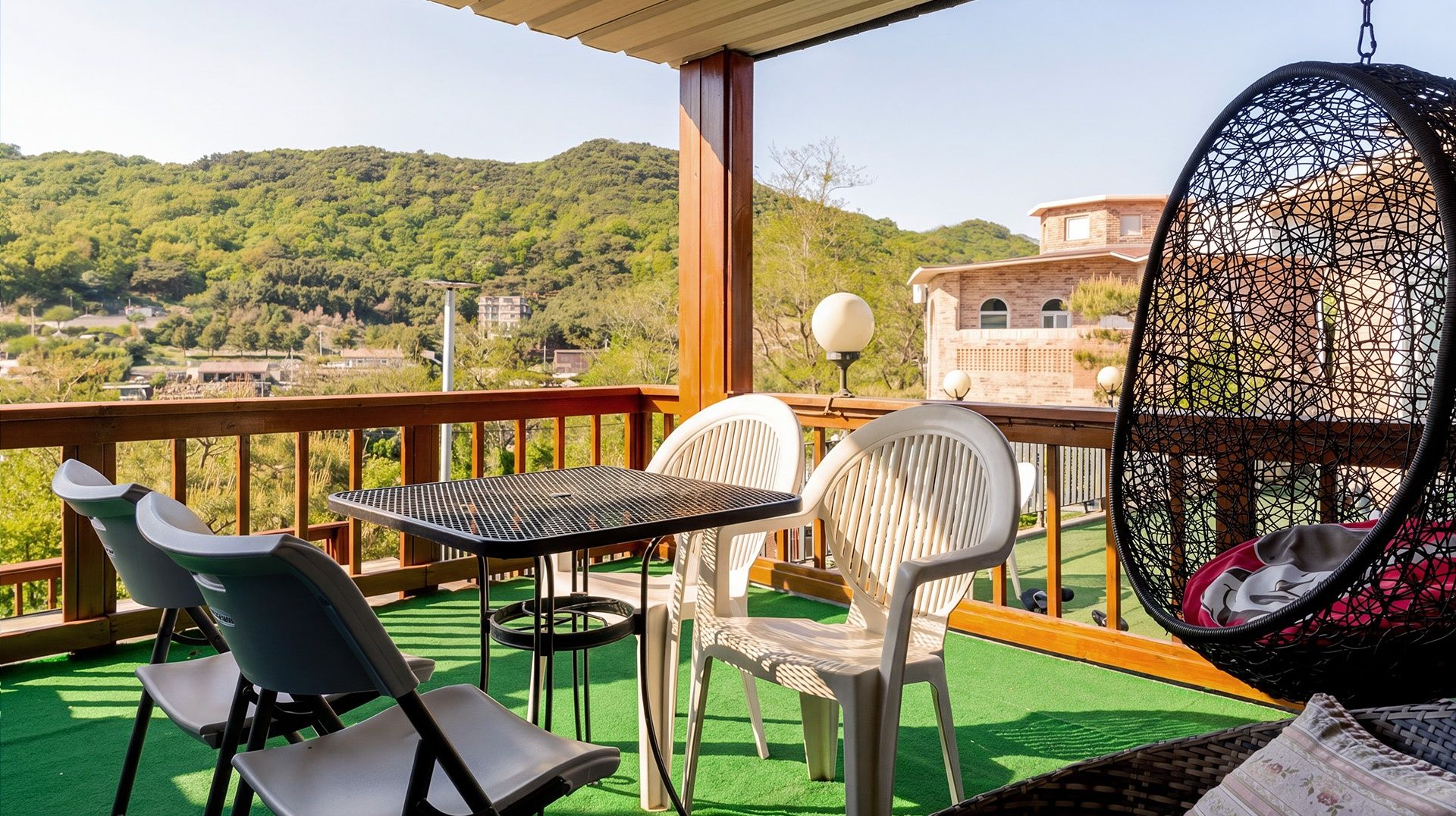 Uma varanda com mesa e cadeiras, uma cadeira suspensa e vista para uma paisagem montanhosa.