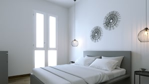 Quarto moderno com uma cama grande, uma mesinha de cabeceira, luminária na parede e uma porta com janela.